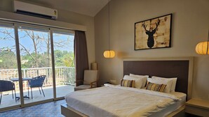 Quarto de hotel com uma cama grande, varanda com cadeiras e vista para árvores.