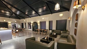 Uma ampla área de estar com pé direito alto, diversos arranjos de assentos incluindo sofás e poltronas, e um espaço bar com balcão.