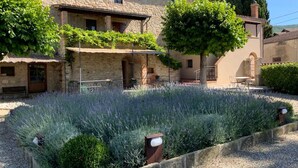 Um edifício de pedra com um pátio, uma pérgula e um jardim bem cuidado com lavanda.