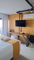 Quarto de hotel com cama, escrivaninha, cadeira, televisão e ar condicionado.