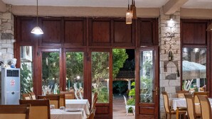 Um restaurante com mesas e cadeiras de madeira, paredes de pedra e grandes janelas.