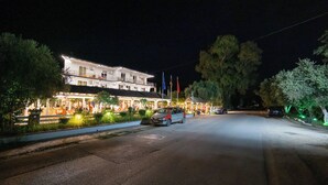 Um hotel com fachada bem iluminada, um carro estacionado na frente e bandeiras no telhado.