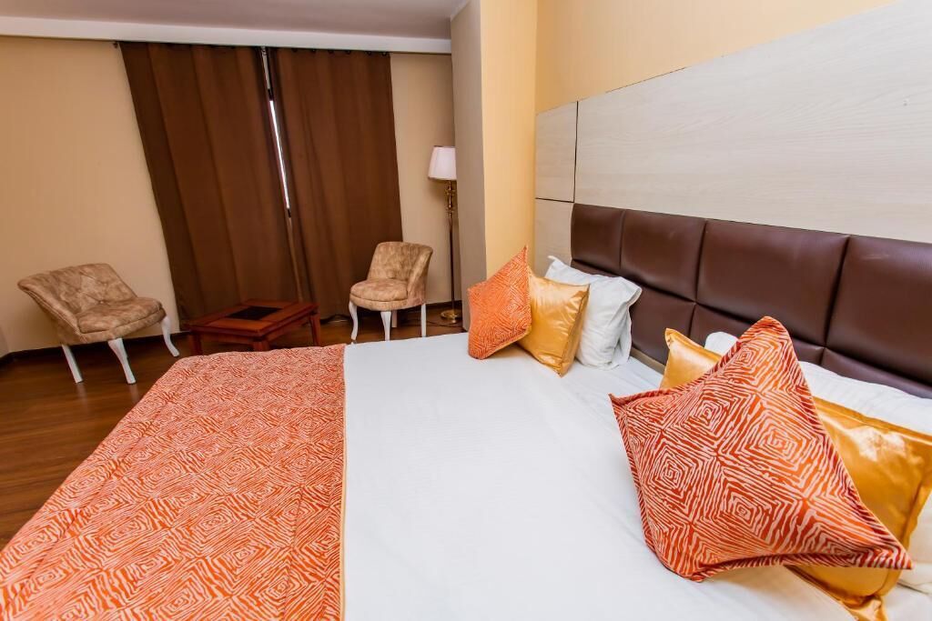 Quarto de hotel com uma cama grande, duas poltronas, uma mesa de cabeceira e um abajur.
