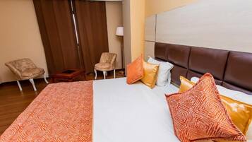 Quarto de hotel com uma cama grande, duas poltronas, uma mesa de cabeceira e um abajur.