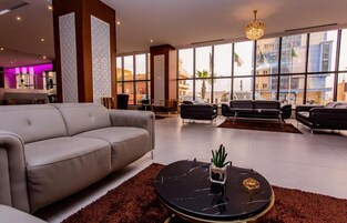 Um hall de hotel moderno com um sofá cinza, poltronas pretas e uma mesa de centro redonda preta com um cacto.