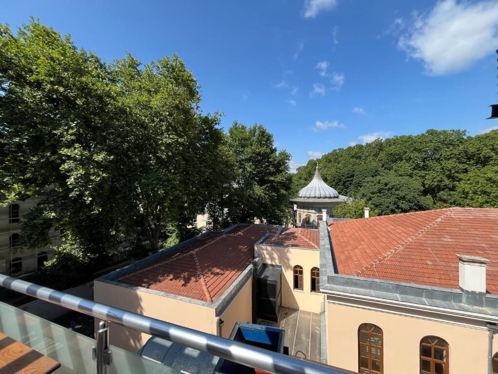 Um edifício com telhado de telhas vermelhas, uma pequena torre com cúpula e um corrimão de vidro em primeiro plano.