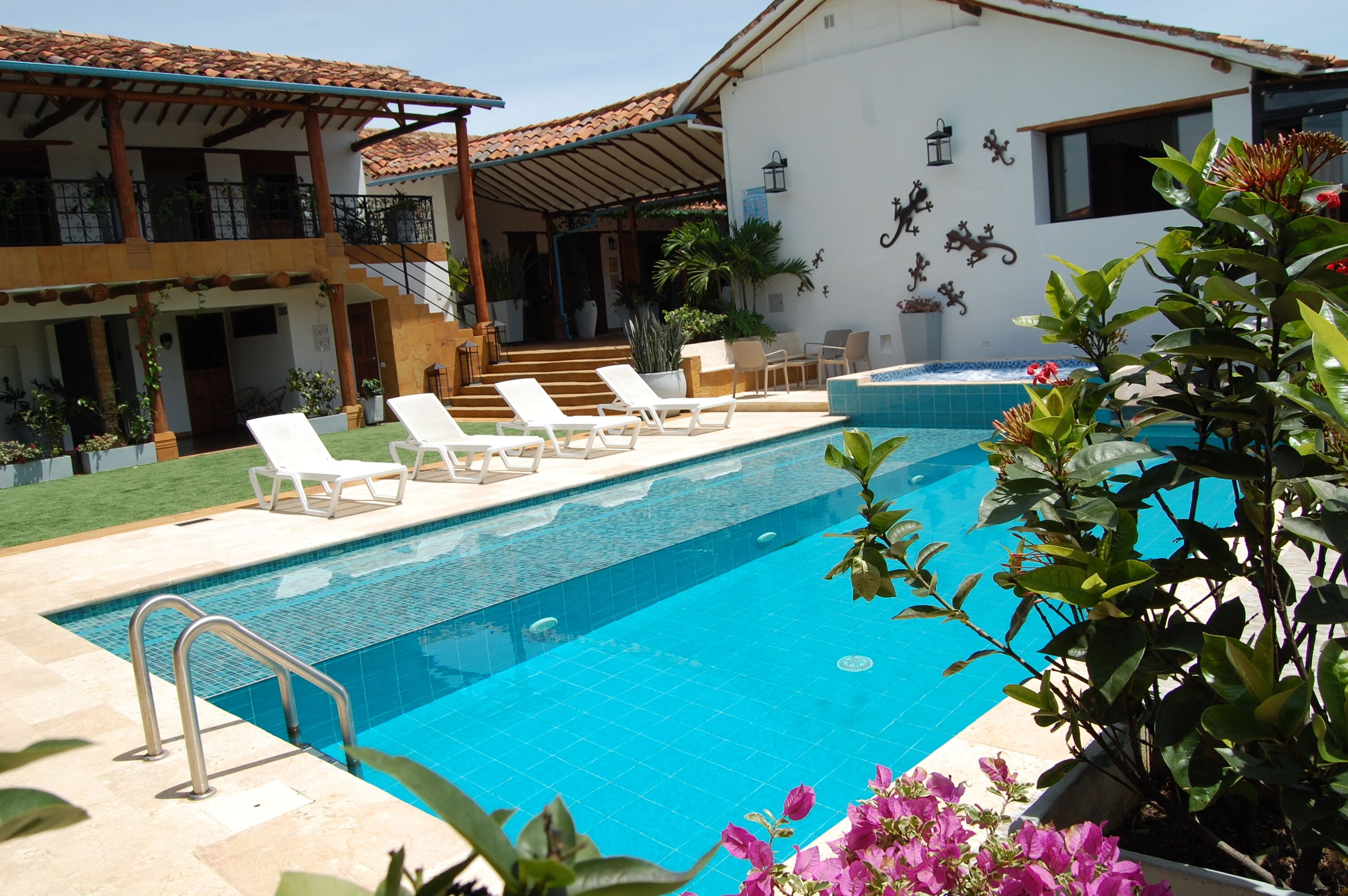 Uma piscina com espreguiçadeiras brancas, um terraço coberto e plantas em vasos.