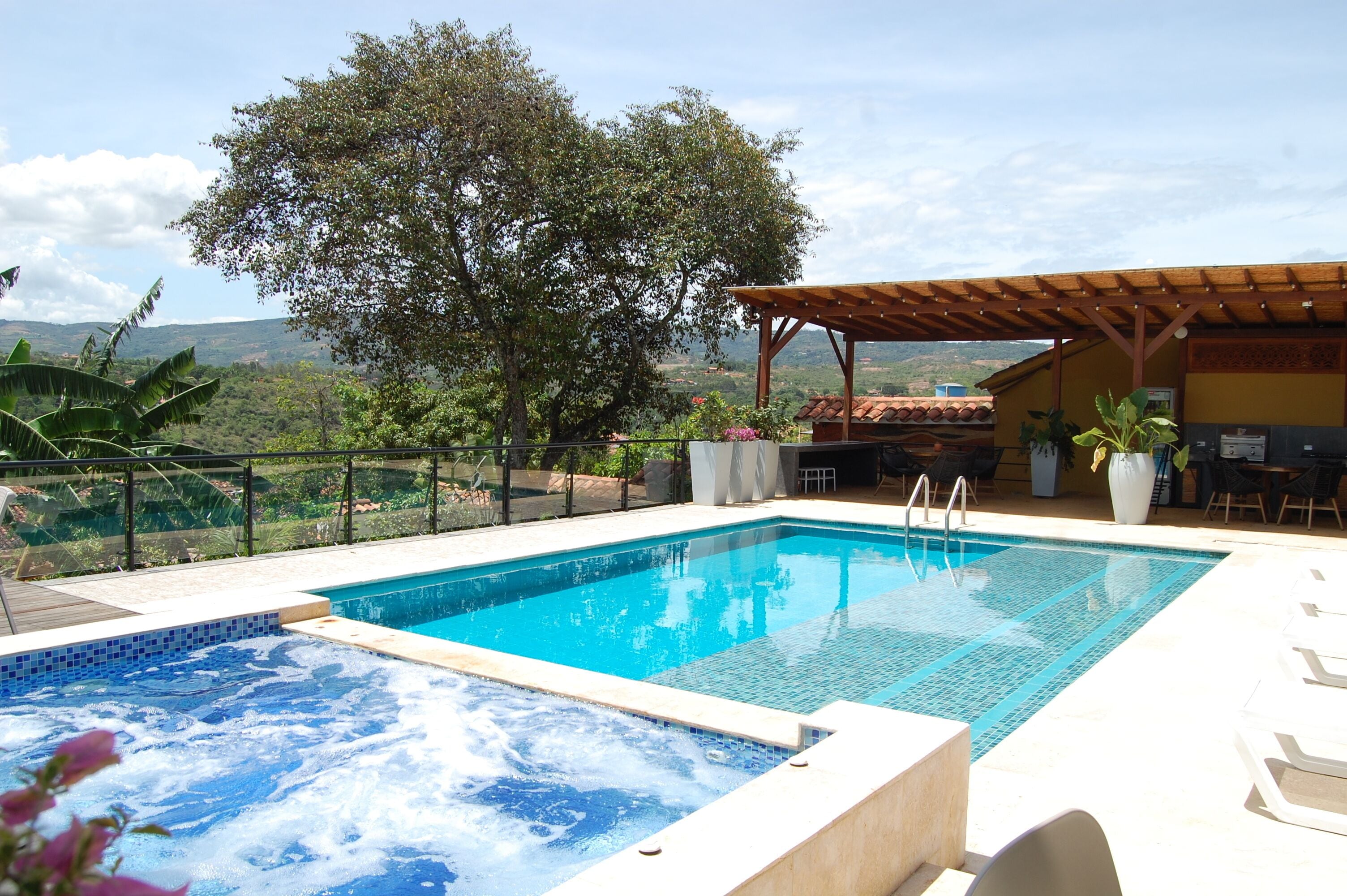 Piscina com hidromassagem, rodeada por um deck com espreguiçadeiras e um pergolado.