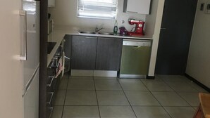 Uma cozinha compacta com geladeira, pia, lava-louças e uma janela com persianas.