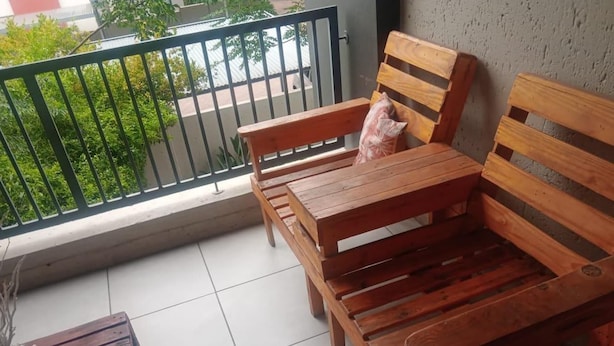 Um banco de madeira com almofada numa varanda com guarda-corpo de metal.
