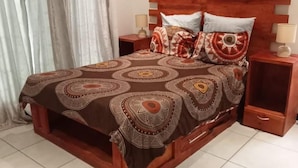 Uma cama com colcha estampada e duas almofadas, com dois mesinhas de cabeceira de madeira e luminárias.