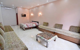 Quarto com cama, sofá e chaise longue. Há uma televisão na parede e um ventilador de teto.