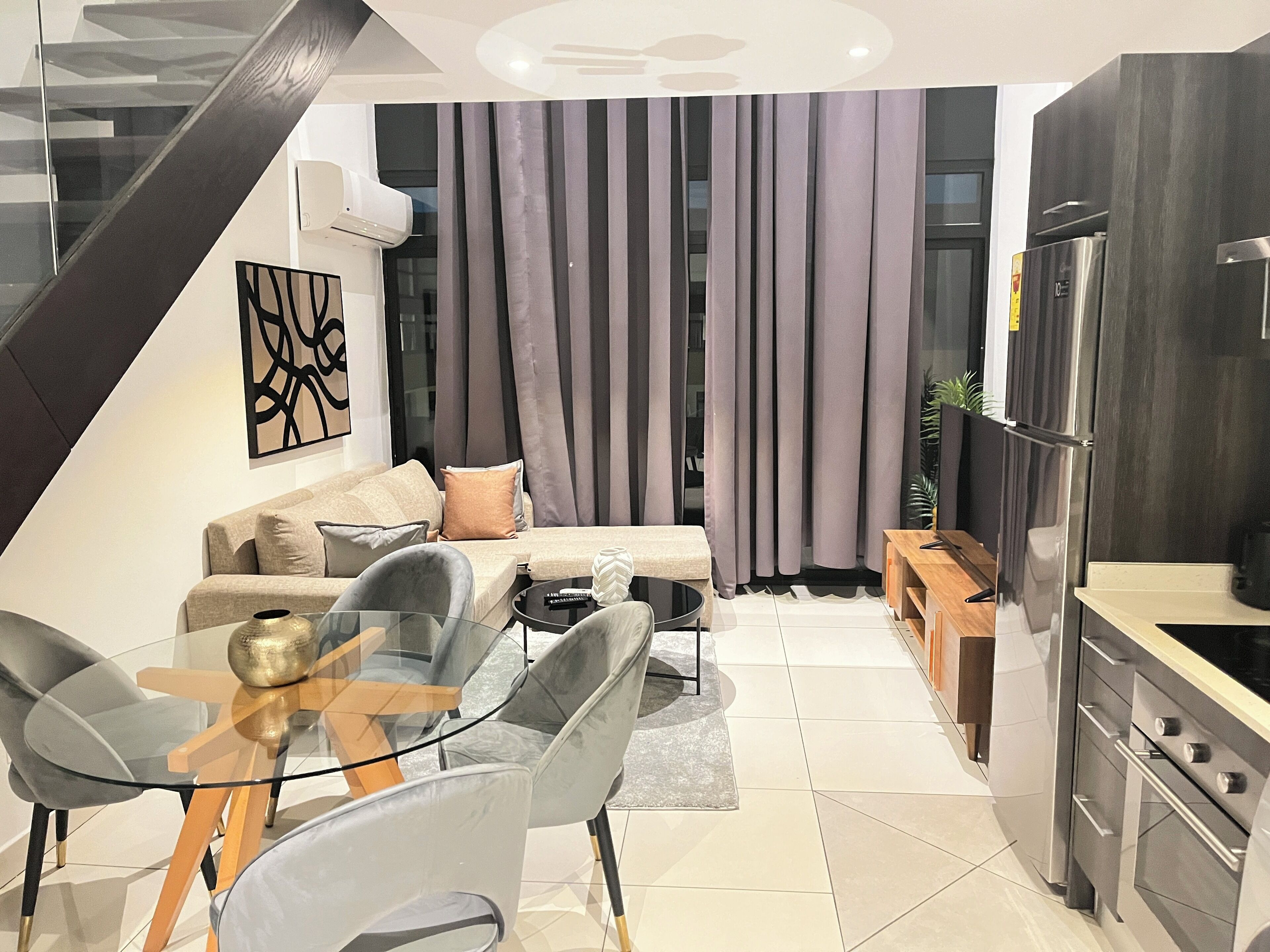 Uma sala de estar moderna com um sofá, uma mesa de centro de vidro e um espaço de jantar com cadeiras e uma mesa de madeira.