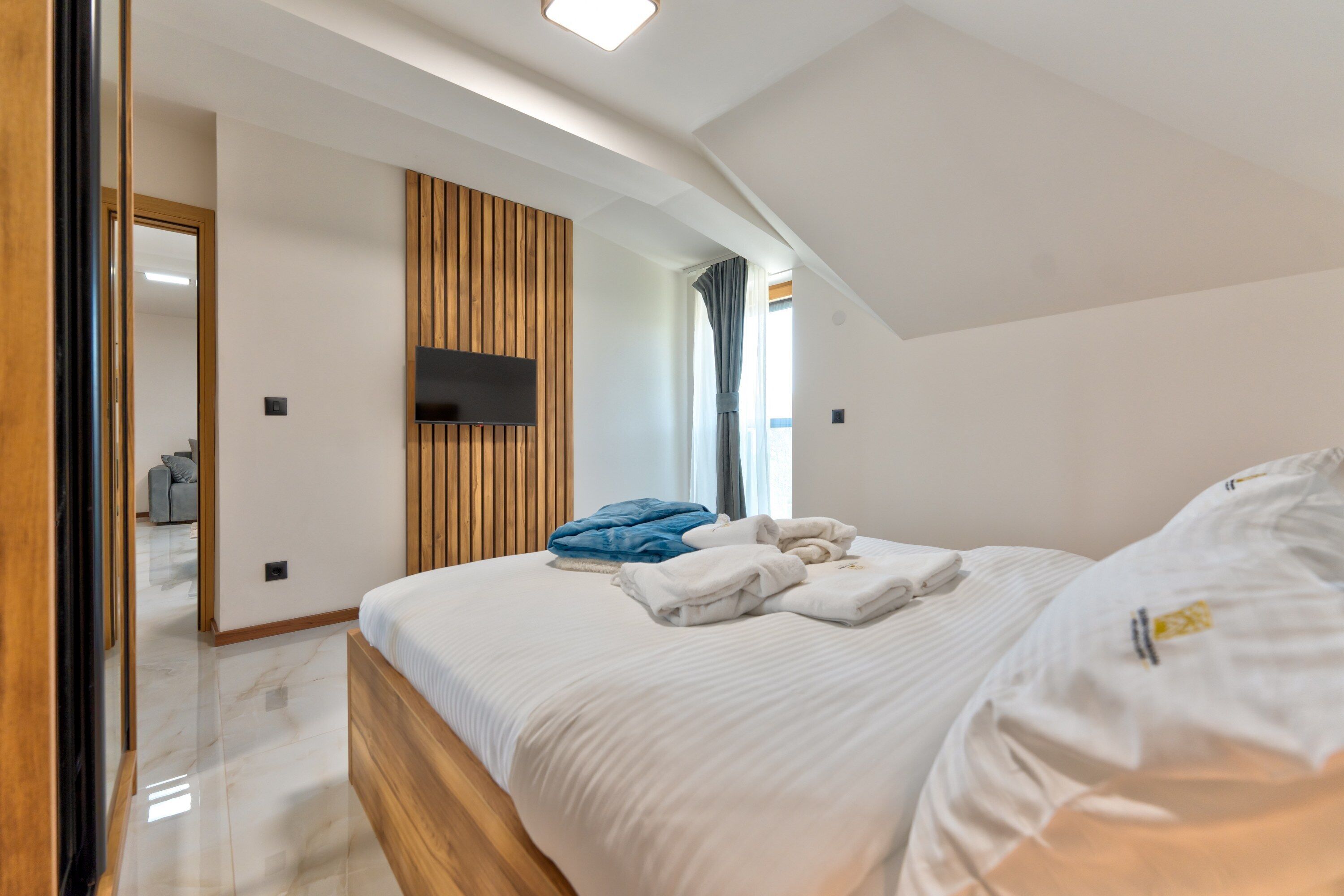 Quarto moderno com uma cama grande, televisão de tela plana na parede e um painel de madeira decorativo.