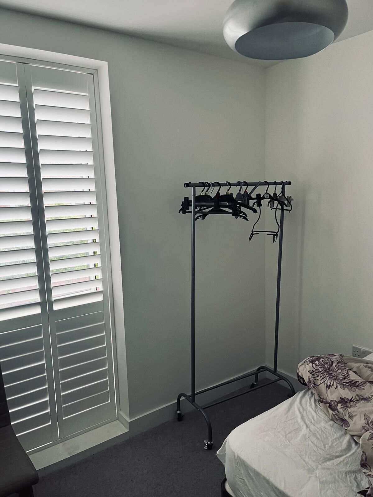 Quarto com cama, um cabideiro e janela com persianas.
