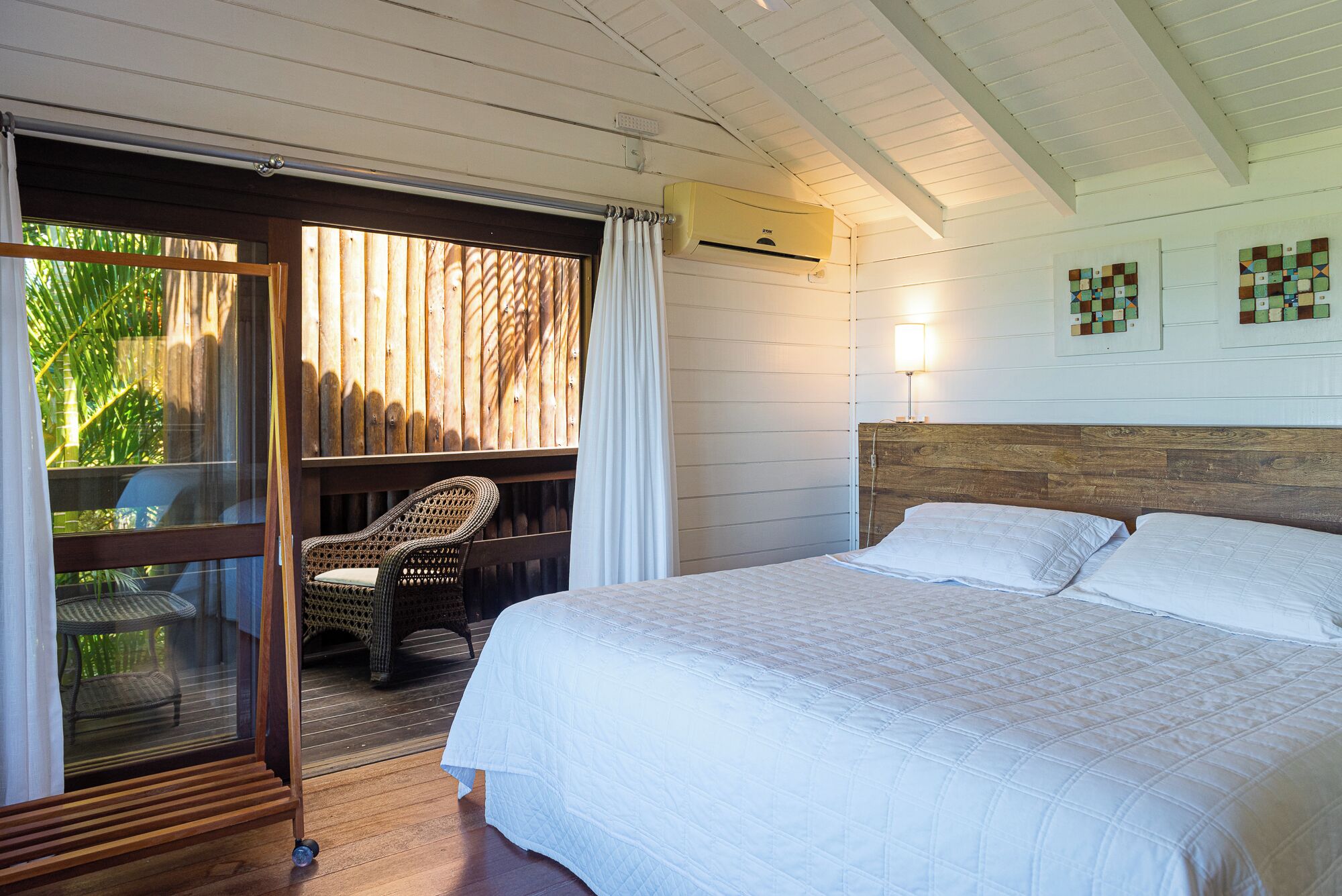 Quarto com cama, uma cadeira e porta de vidro deslizante que dá para uma área externa.