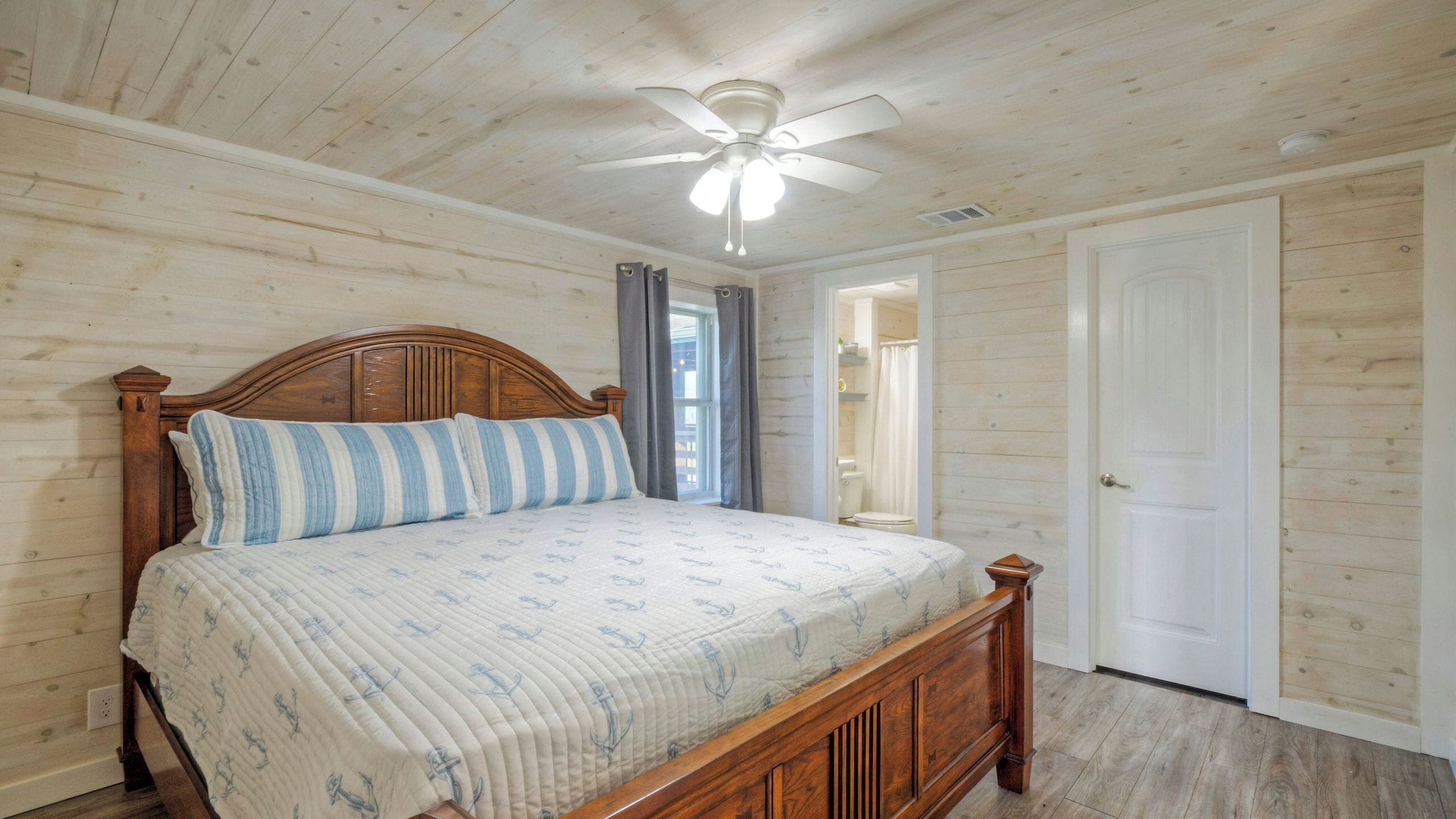 Quarto com cama de madeira, ventoinha no teto e porta branca.