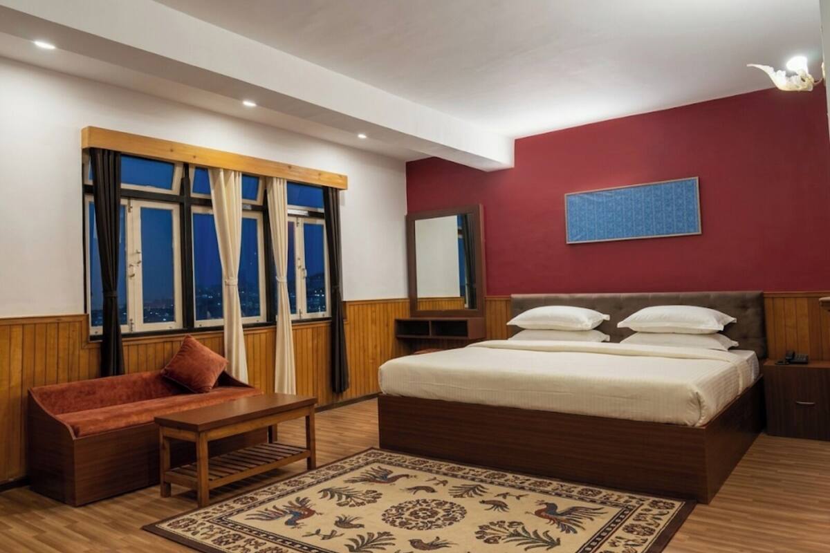 Quarto com cama, escrivaninha, cadeira, janela com cortinas, espelho e obra de arte na parede.