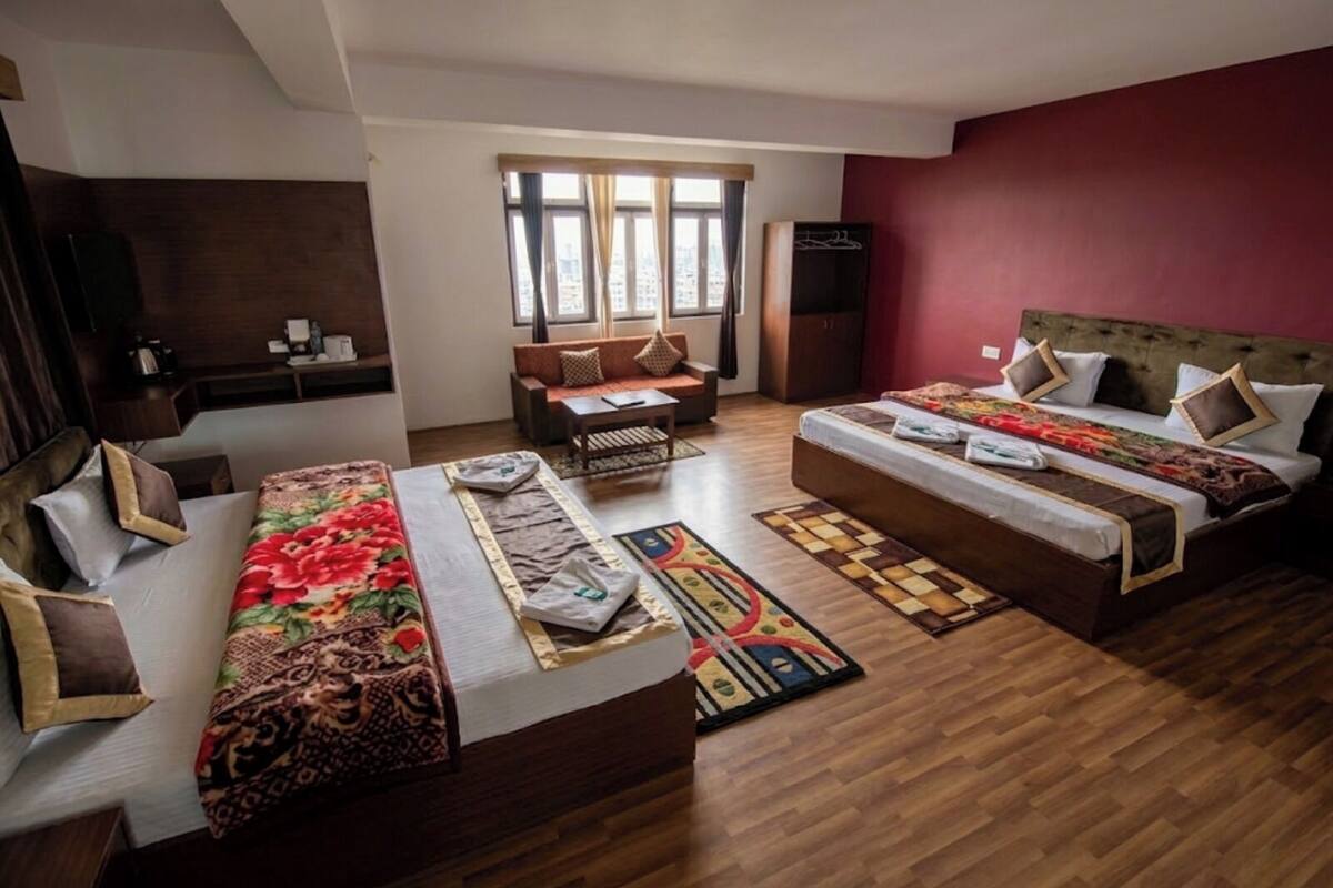 Quarto de hotel com cama, sofá, escrivaninha, guarda-roupa e uma grande janela.