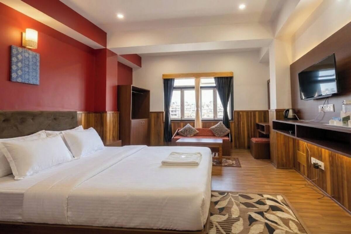 Quarto de hotel com uma cama grande, uma mesa, uma televisão e uma janela com cortinas.