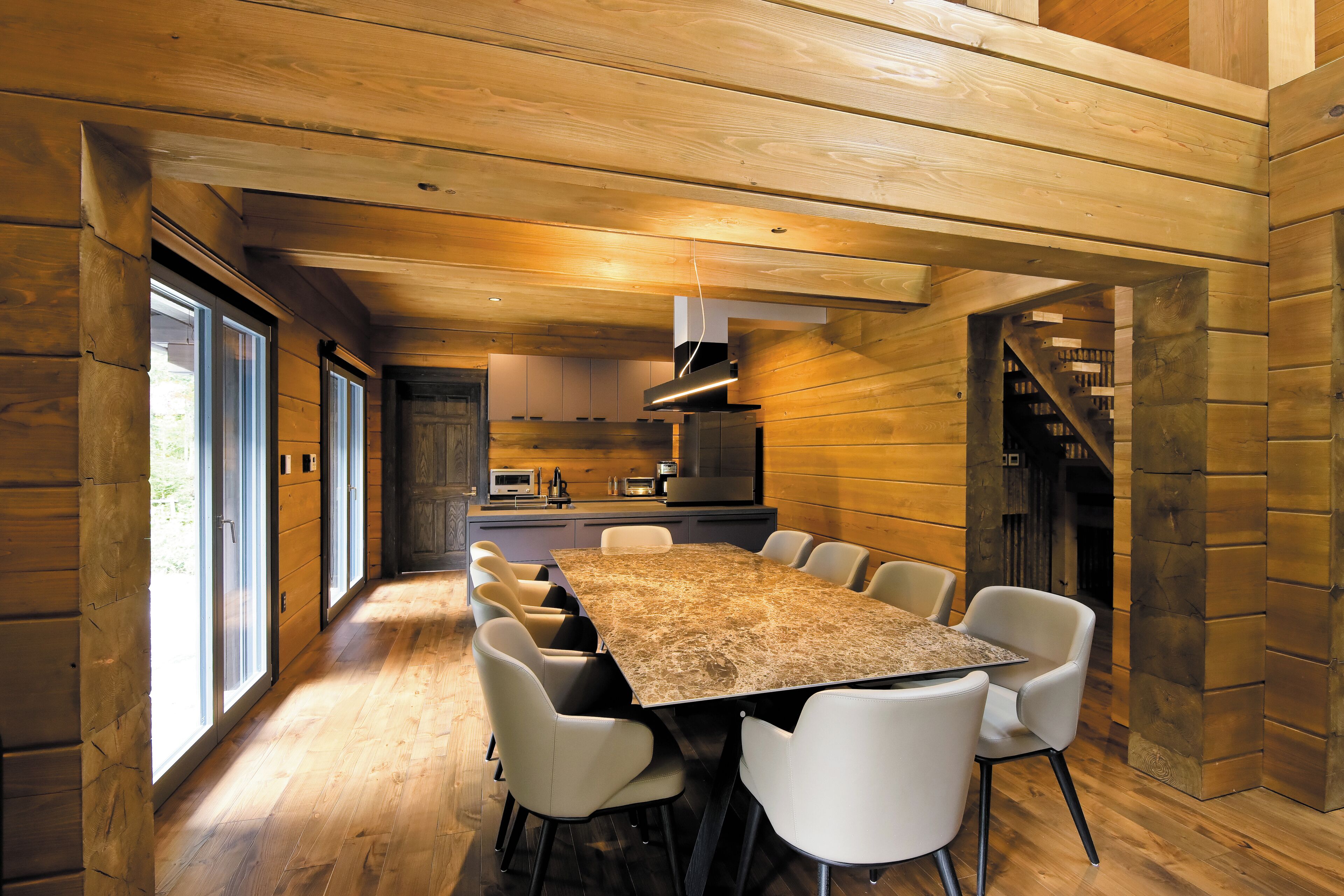 Um interior moderno com uma mesa de jantar de madeira, rodeada por cadeiras, uma área de cozinha com micro-ondas e uma escadaria para outro andar.