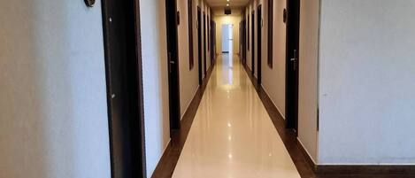 Um corredor longo e bem iluminado, com portas em ambos os lados, que leva a um quarto claro no final.