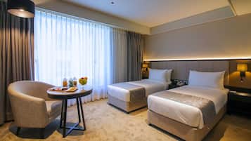 Quarto de hotel com duas camas, uma mesa pequena com lanches e uma cadeira.