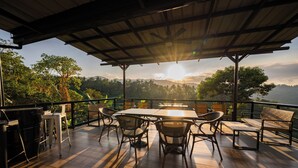 Um pátio externo com mesa e cadeiras, churrasqueira e vista da paisagem ao redor.