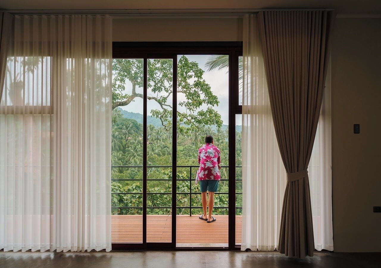 Quarto com uma grande porta de vidro deslizante que dá para uma varanda com vista para áreas verdes e colinas.