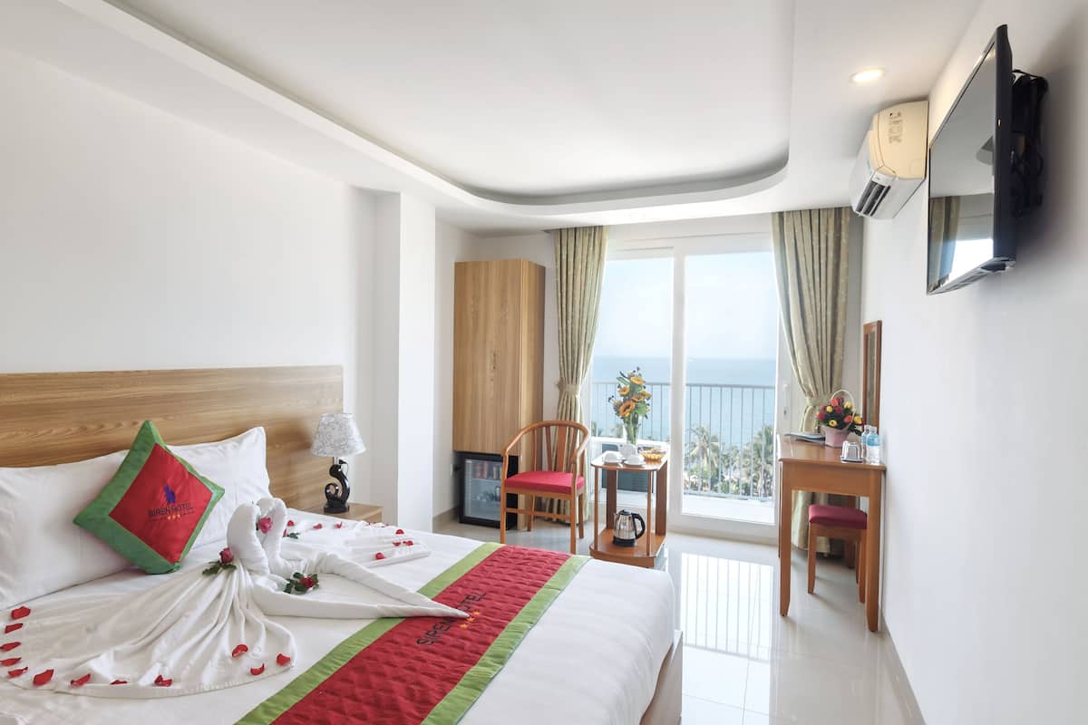 Quarto de hotel com cama, escrivaninha, cadeira, televisão e vista para o mar.
