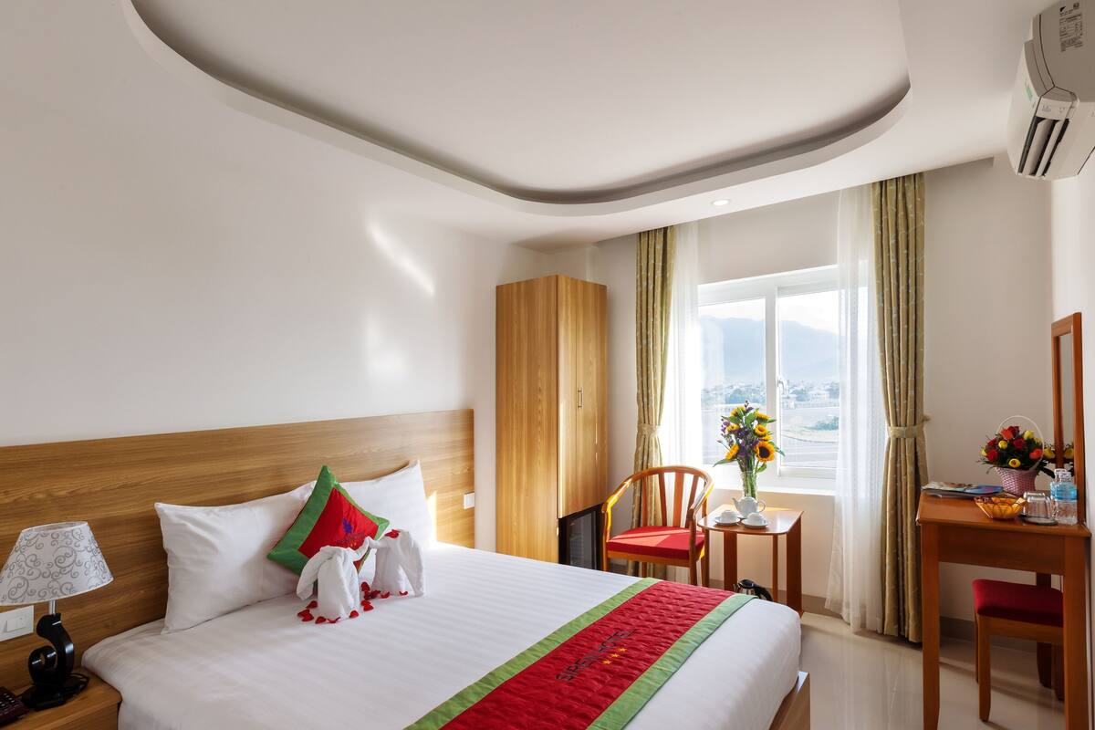 Quarto de hotel com cama, escrivaninha, cadeira, janela com vista e armário.