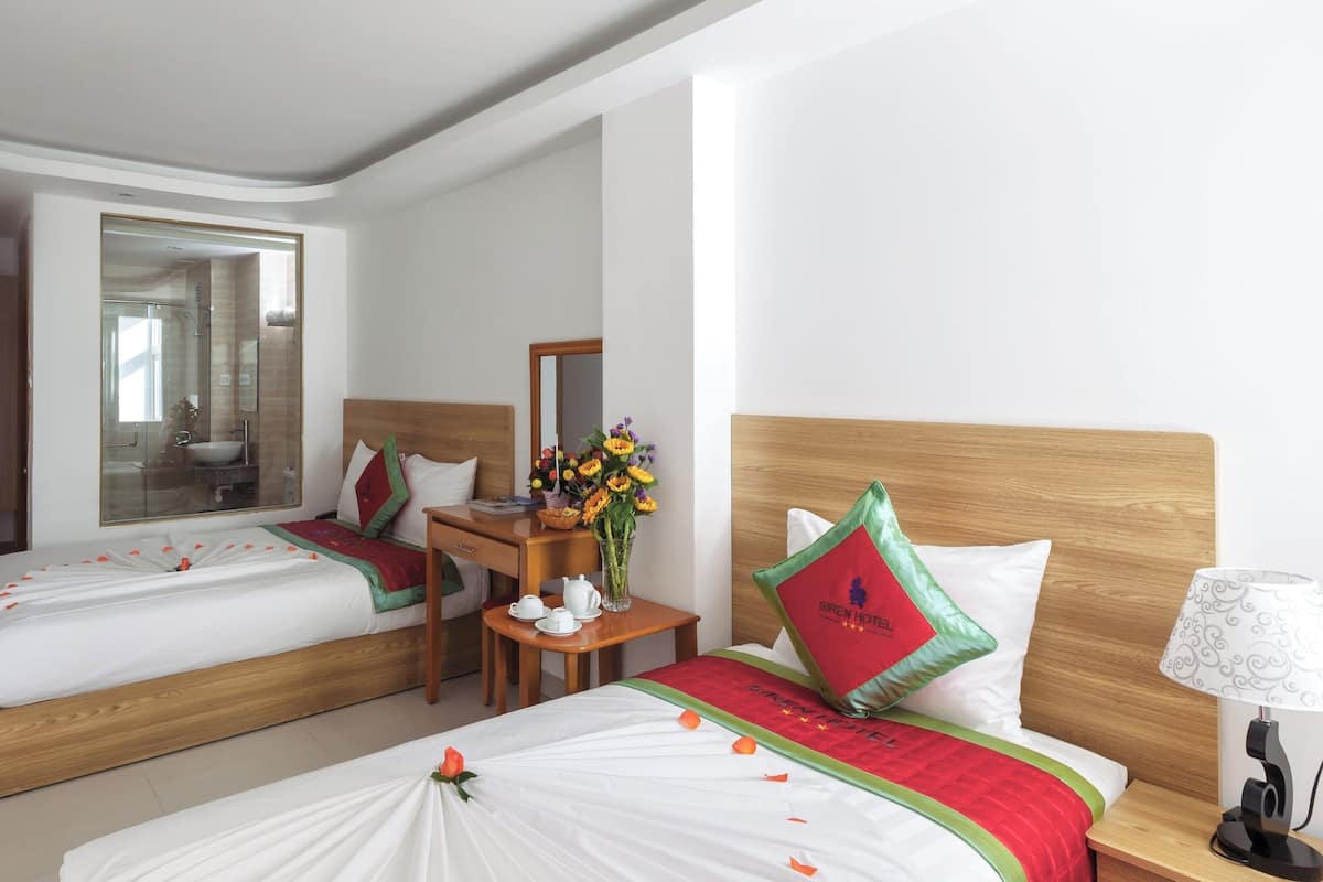 Quarto de hotel com duas camas, uma escrivaninha, uma TV e um espelho.