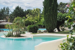 Uma área de piscina com espreguiçadeiras, uma palmeira e uma conífera alta.