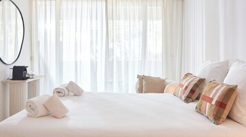 Quarto de hotel com uma cama grande, uma mesa de cabeceira com máquina de café e cortinas translúcidas.