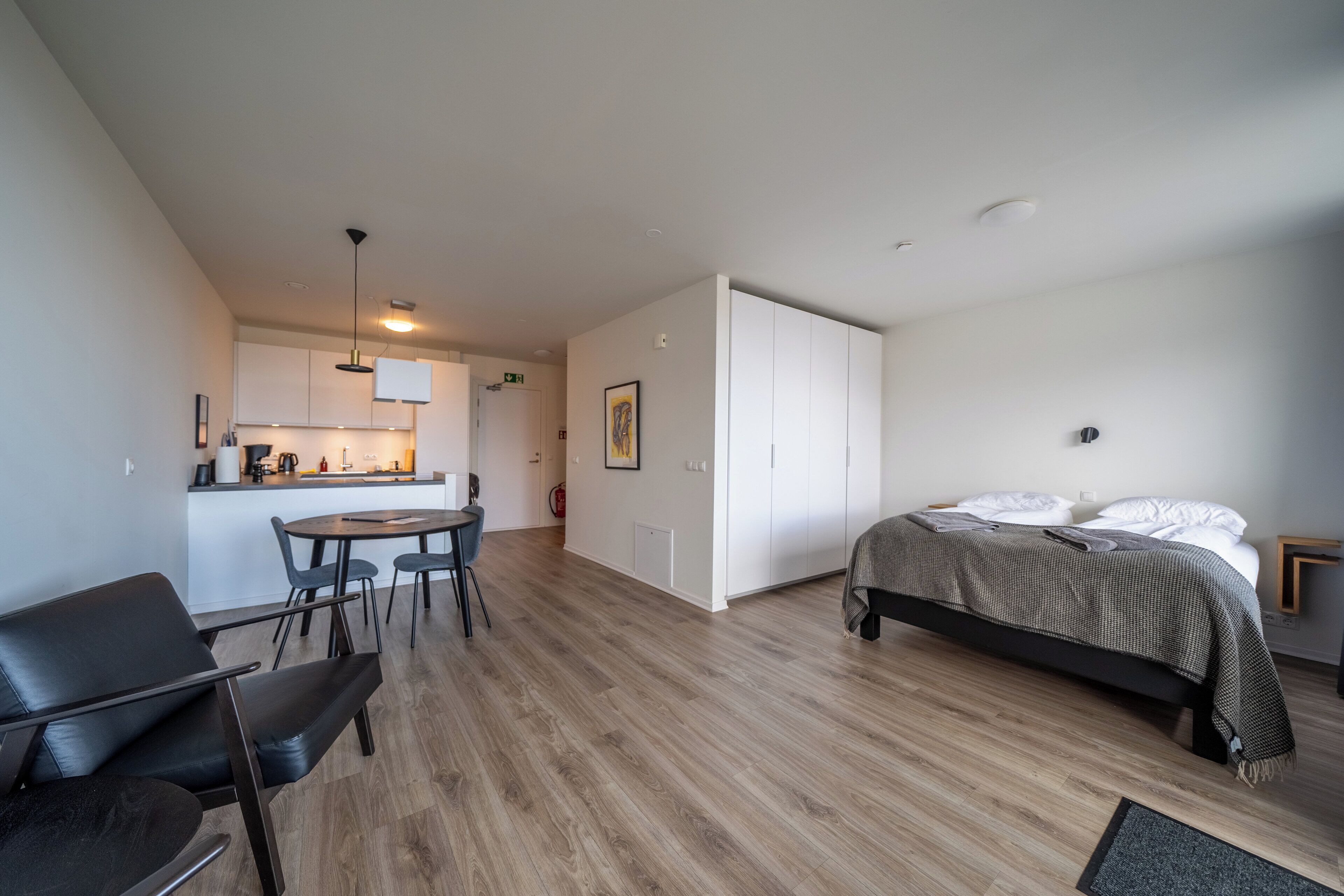 Quarto de hotel moderno com cama, secretária e cozinha compacta.