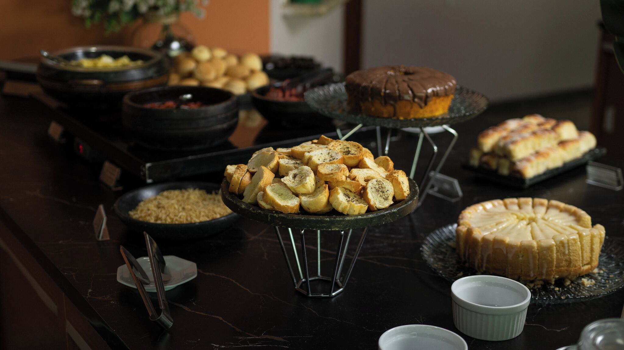 Uma mesa de buffet com diversos pratos, incluindo pão, uma torta e um doce coberto com chocolate.