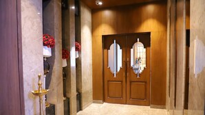 Um corredor com piso de mármore, um abajur de latão tradicional e uma porta de madeira com um espelho.