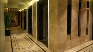 Um corredor com piso de mármore, um vaso de planta e várias portas de elevador.