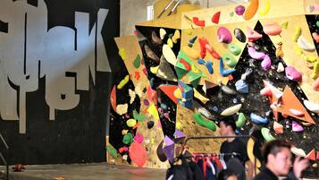 Uma parede de escalada com vários apoios de cores diferentes e uma grande parede preta com letras brancas.