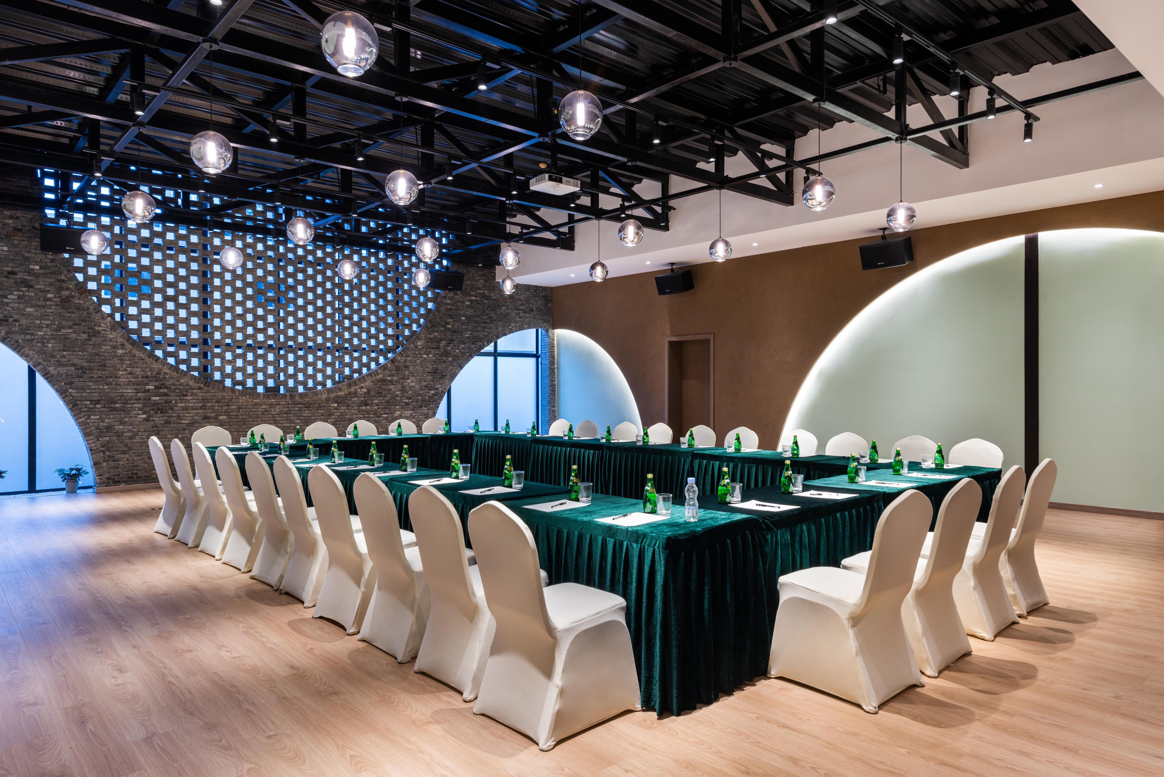Sala de conferência com várias mesas, cadeiras brancas e design moderno no teto.