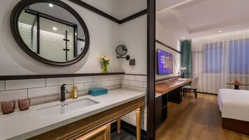 Quarto de hotel com banheiro, escrivaninha, cama e televisão.