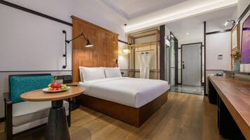 Quarto de hotel com uma cama, uma mesinha com frutas, uma cadeira, um armário de madeira e um espelho.