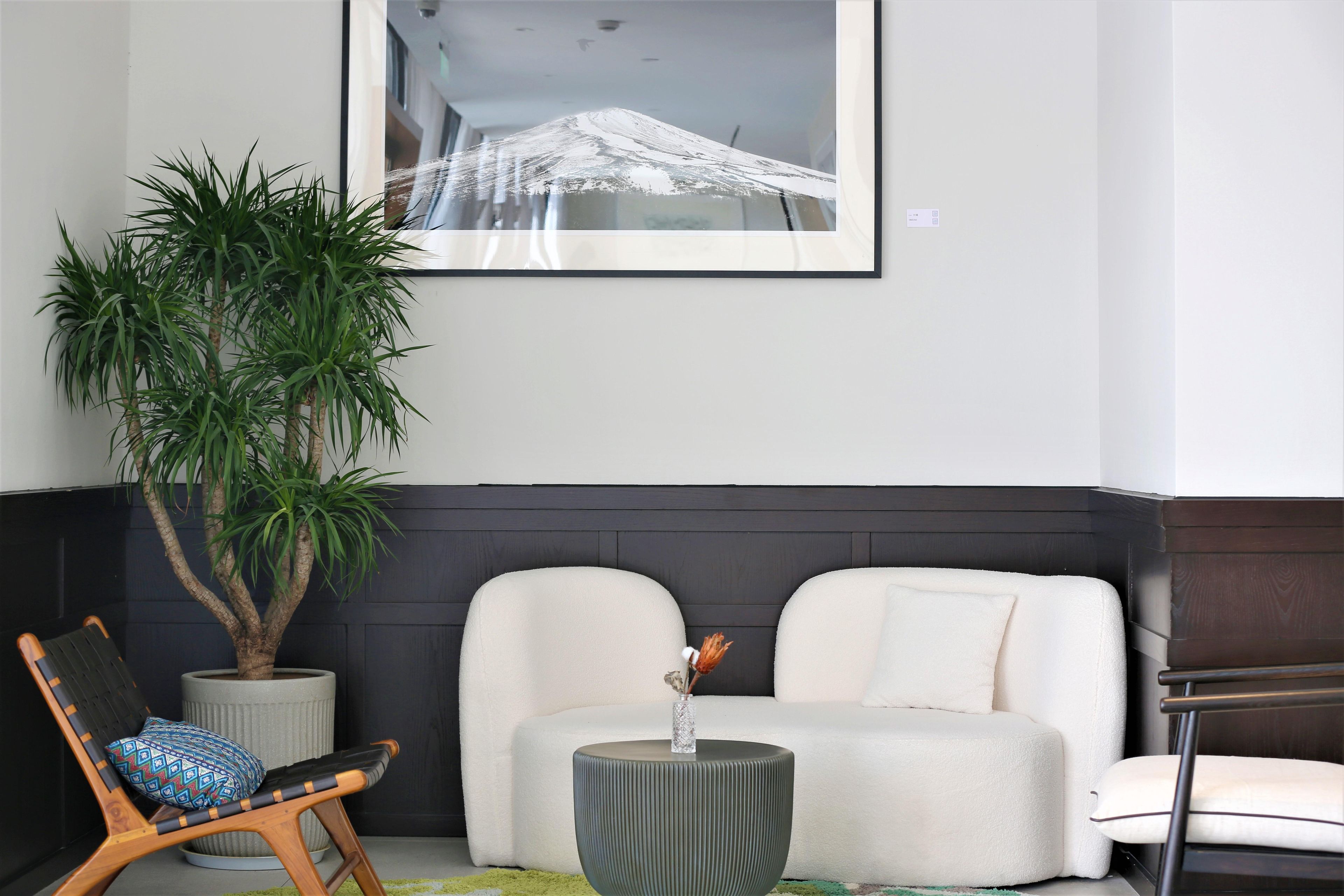 Uma sala de estar moderna com uma planta grande em vaso, uma obra de arte emoldurada e um sofá com uma mesinha lateral.