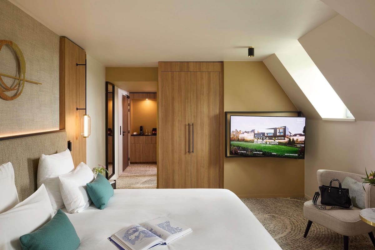 Quarto de hotel com cama, televisão, escrivaninha e vista para o exterior do hotel.