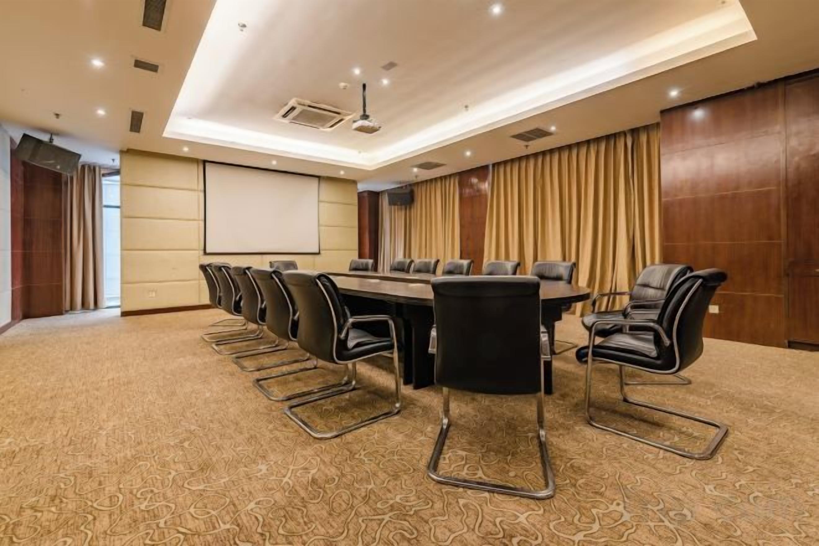 Uma sala de conferências com uma mesa comprida, várias cadeiras, uma tela de projetor e piso carpeteado.