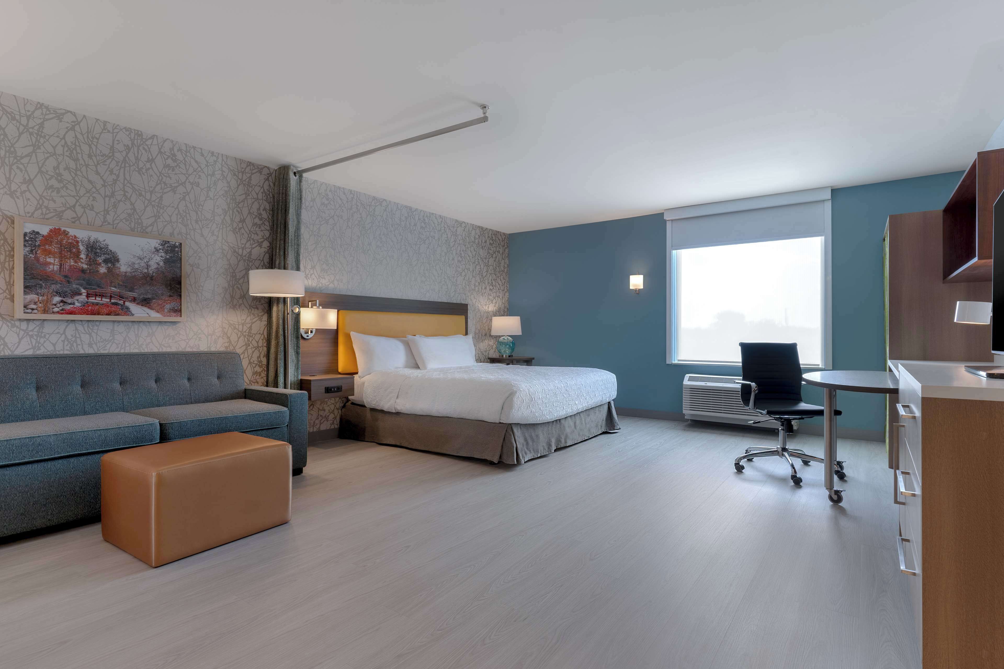Quarto de hotel moderno com cama, sofá, escrivaninha e uma grande janela.