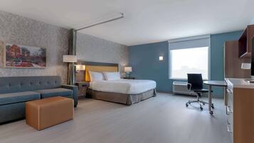 Quarto de hotel moderno com cama, sofá, escrivaninha e uma grande janela.