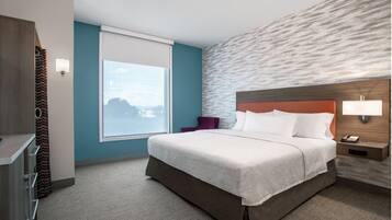 Quarto de hotel moderno com uma cama grande, uma mesa de cabeceira com abajur, uma janela com vista e um espaço para o banheiro.