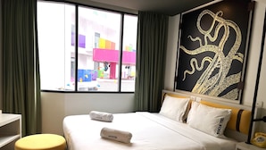 Quarto de hotel com uma cama, uma janela com cortinas, um banquinho amarelo e uma parede com design preto e dourado.