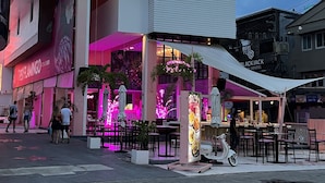 Um edifício com uma placa indicando 'SOCIA TEL' e um restaurante chamado 'TST FLAMINGO' com mesas ao ar livre.